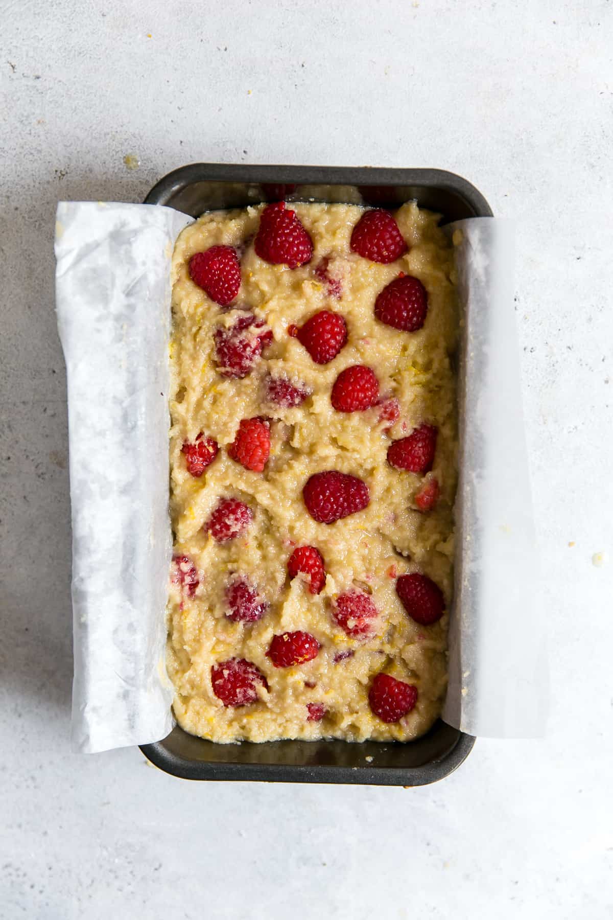 lemon raspberry bread batter in loaf pan with parchment paper overhang